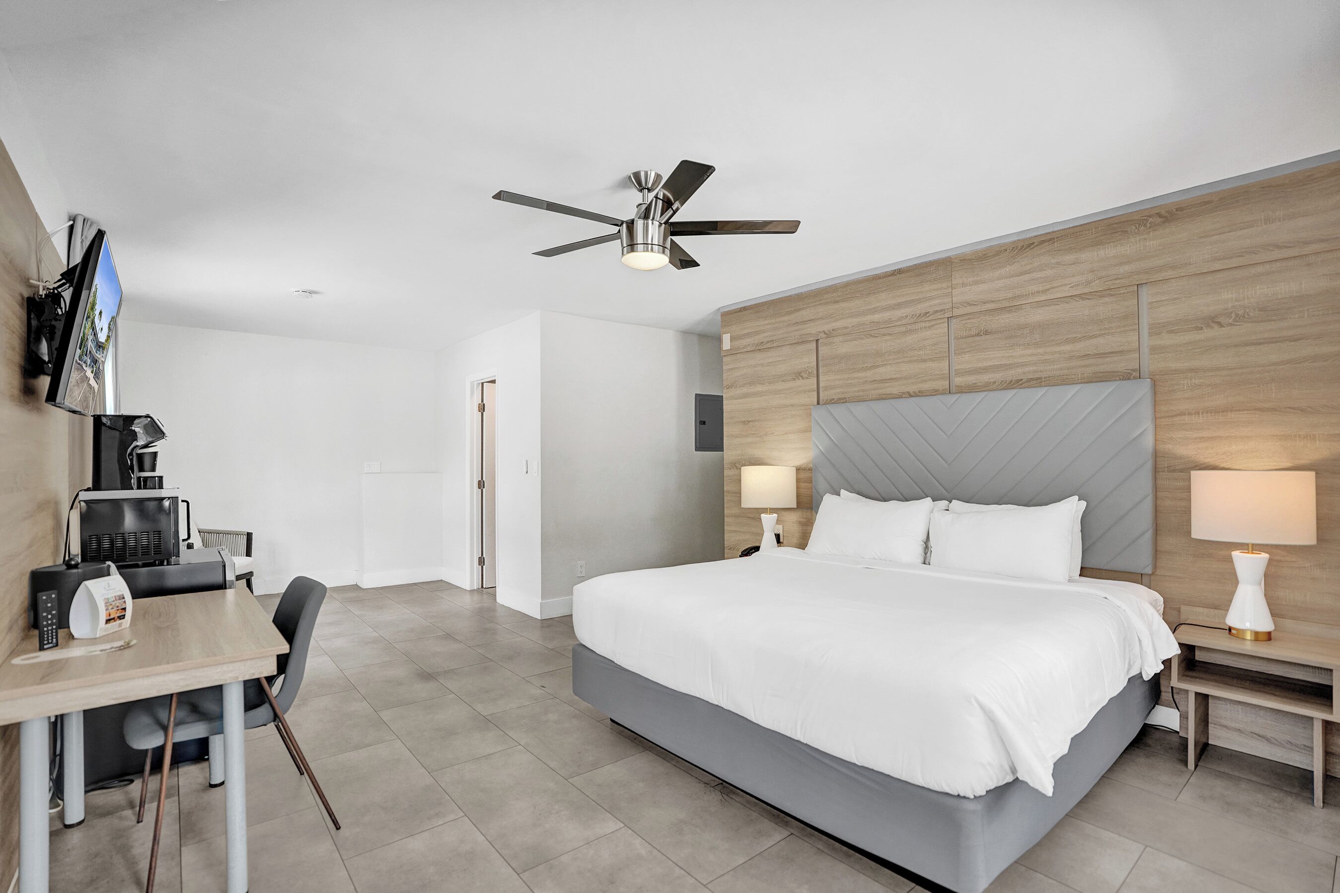 Quarto de hotel com cama, escrivaninha, cadeira, ventoinha no teto e uma parede de destaque em madeira.