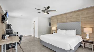Quarto de hotel com cama, escrivaninha, cadeira, ventoinha no teto e uma parede de destaque em madeira.