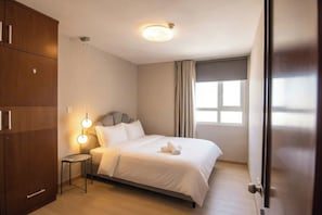 Quarto de hotel com cama, guarda-roupa, mesa de cabeceira com abajur e janela com cortinas.