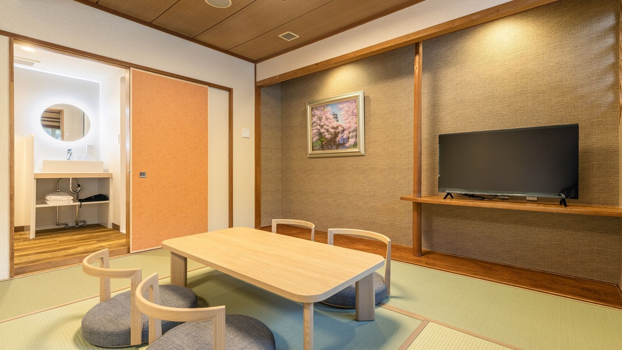 Um quarto tradicional japonês com tatame, uma mesa baixa e uma televisão sobre um suporte de madeira.