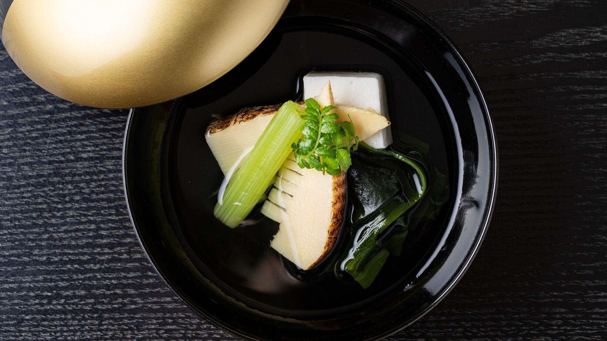 Uma tigela preta com um alimento branco, vegetais verdes e um objeto amarelo.