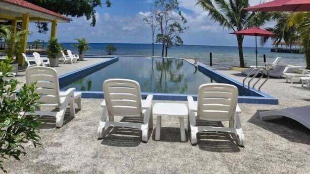Uma área de piscina com espreguiçadeiras, uma barreira de vidro e vista para o mar.