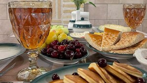 Uma mesa posta com chá, frutas, pão e panquecas.