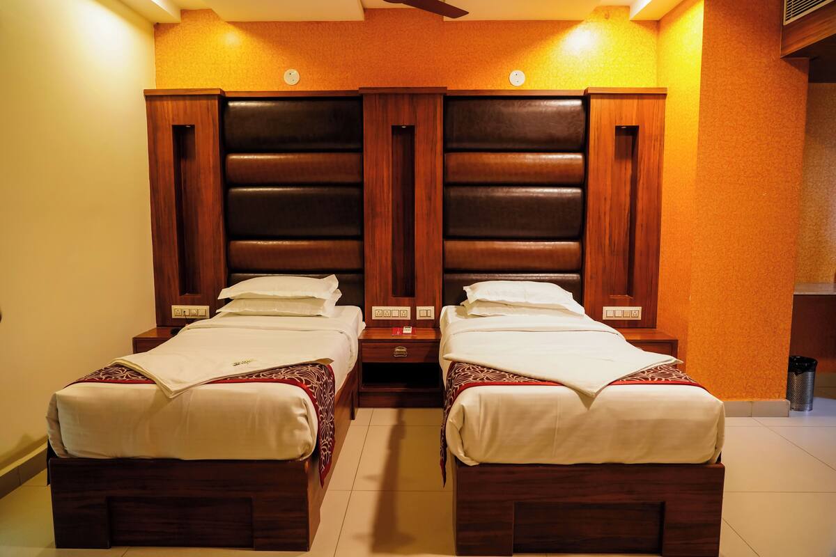 Quarto com duas camas, cabeceiras de madeira, mesas de cabeceira e um cesto de lixo.