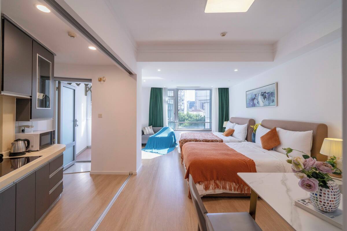 Quarto de hotel moderno com cozinha compacta, uma cama grande, um sofá e vista para a cidade.