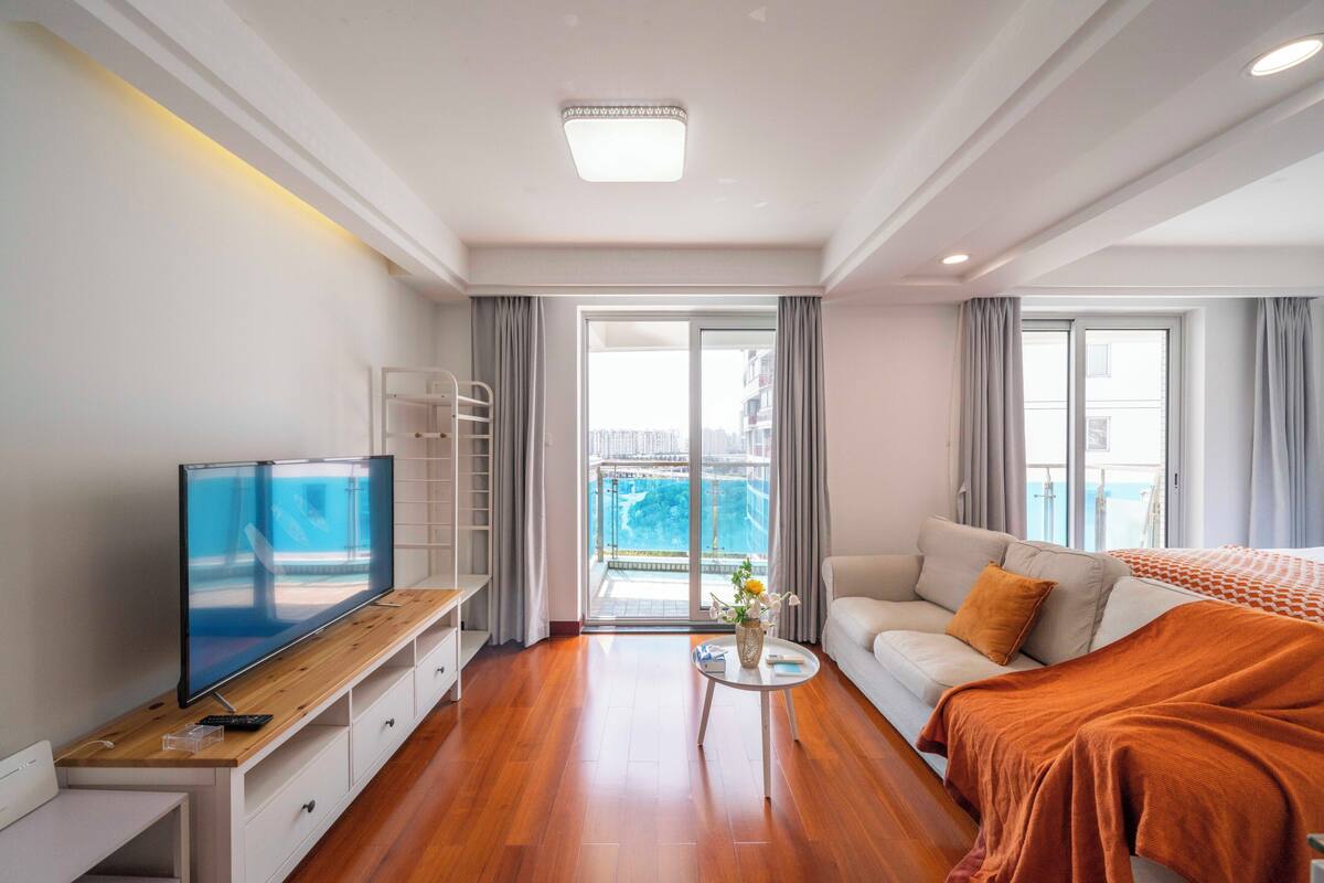 Quarto de hotel moderno com televisão de tela plana, sofá, mesa de centro e varanda com vista.