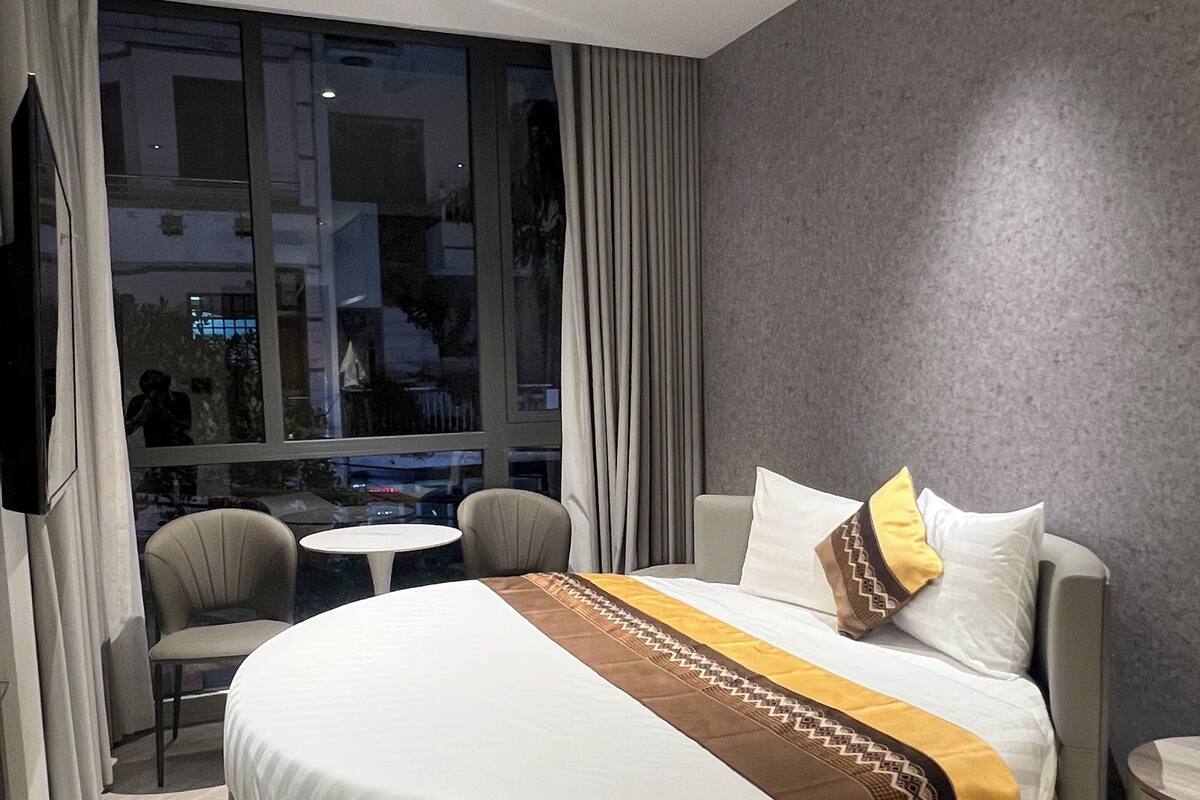 Quarto de hotel moderno com uma cama redonda, uma mesa pequena e área de estar com uma cadeira.
