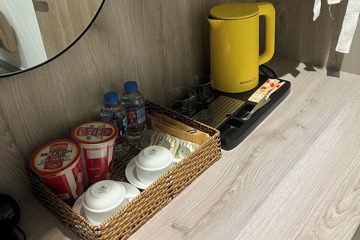 Quarto de hotel com piso de madeira, caneca amarela, cesta com alimentos e um espelho.