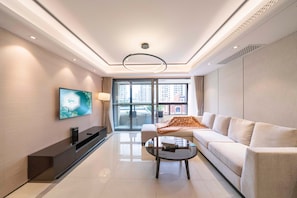 Uma sala de estar moderna com sofá, mesa de centro, TV e vista para a cidade pela janela.