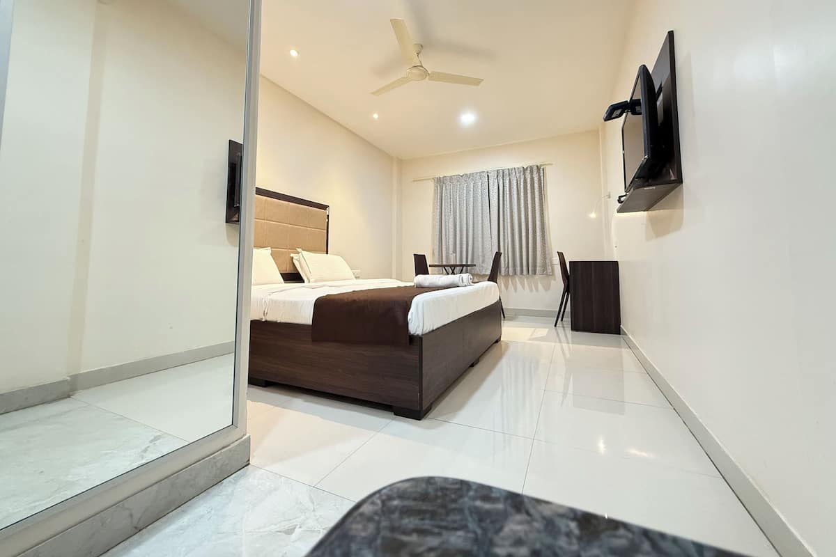 Quarto de hotel moderno com cama, TV, ventoinha no teto e janela com cortinas.