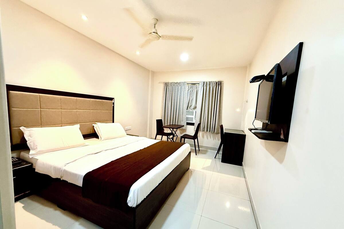 Quarto de hotel com cama, escrivaninha, cadeira, televisão e ventoinha no teto.