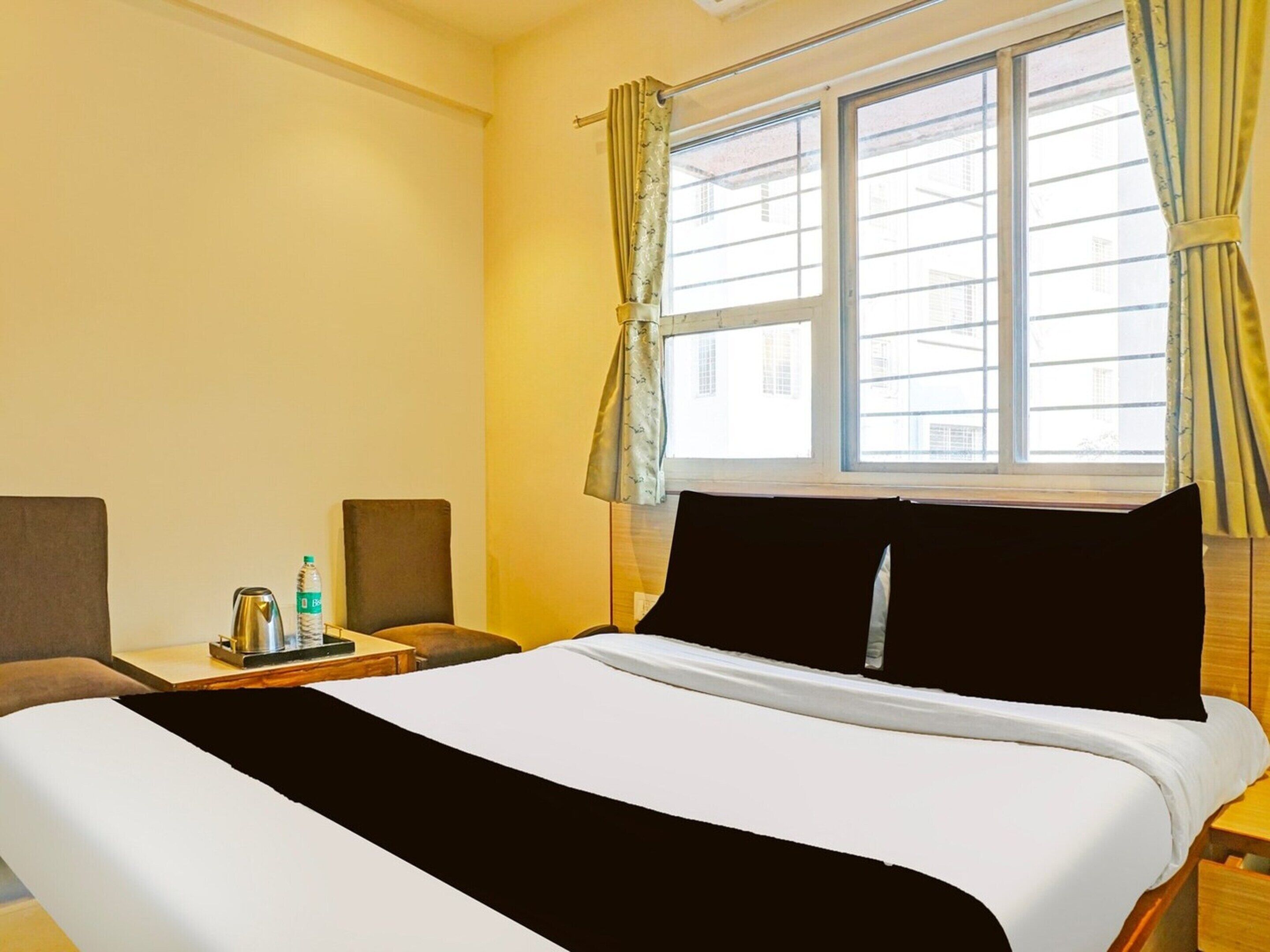 Quarto de hotel com uma cama, uma escrivaninha com cadeira, uma janela com cortinas e vista para edifícios.