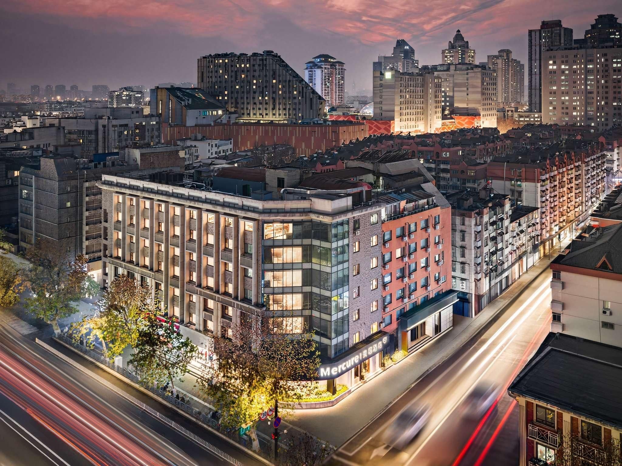 Um hotel de vários andares com design moderno, situado em ambiente urbano com vista para o horizonte da cidade ao entardecer.