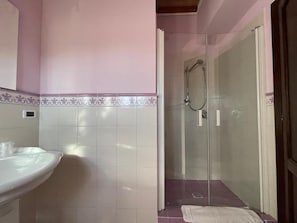 Casa de banho com chuveiro em cabine de vidro, lavatório branco e azulejos decorativos.