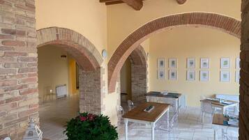 Interior com arcos de tijolo, área de refeições com cadeiras transparentes e quadros nas paredes.