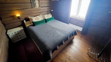 Quarto de cabana de tronco aconchegante, com cama, mesa de cabeceira, luminária na parede e janela.