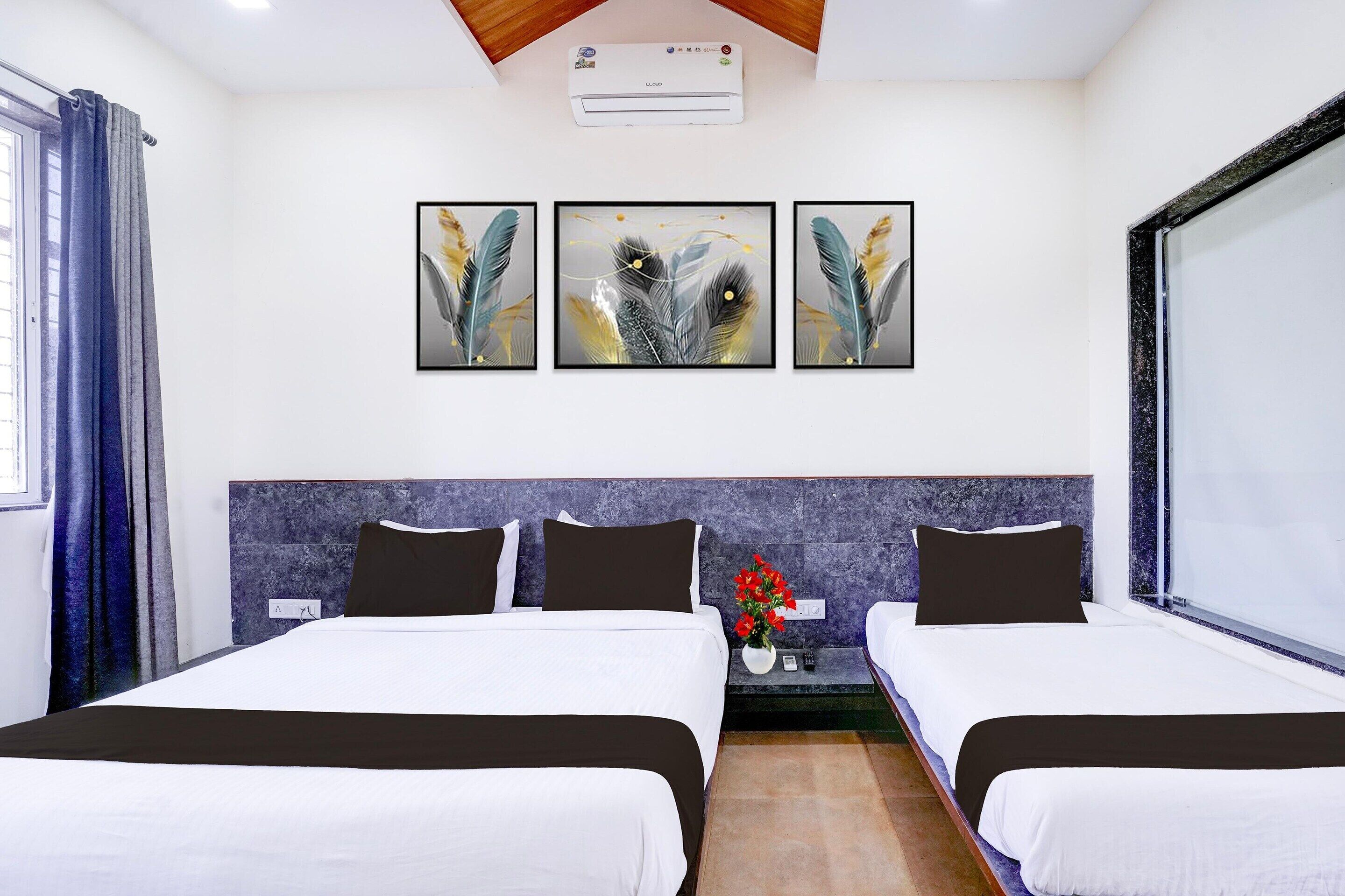 Quarto de hotel com duas camas, cabeceira de mármore, ar condicionado fixado na parede e três obras de arte com penas.