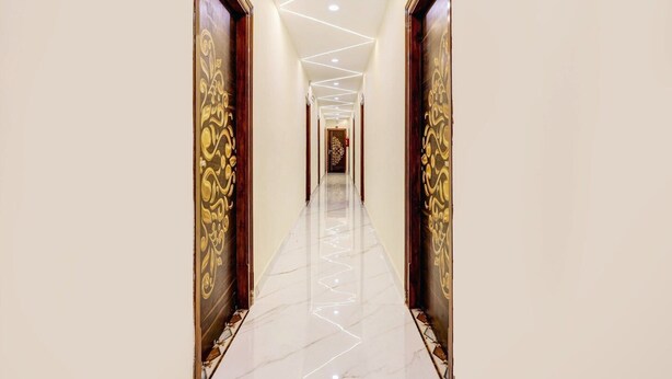 Um corredor com piso de mármore, portas ornamentadas e iluminação embutida.