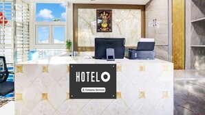 Uma receção de hotel com um letreiro a dizer 'HOTELO Company-Serviced', um computador de mesa e um ventilador de teto.