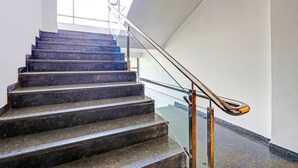 Uma escadaria com degraus escuros e corrimão de vidro.