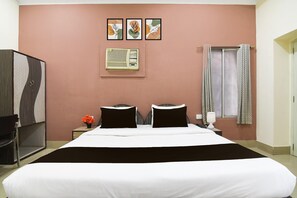 Quarto de hotel com cama, mesa de cabeceira, luminária, janela com cortinas, ar-condicionado fixado na parede e obras de arte emolduradas.