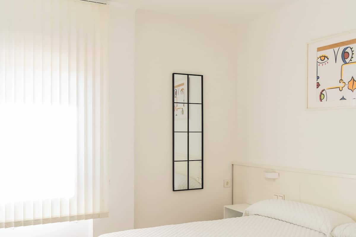Quarto com duas camas, mesa de cabeceira, prateleira na parede e janela com persianas.