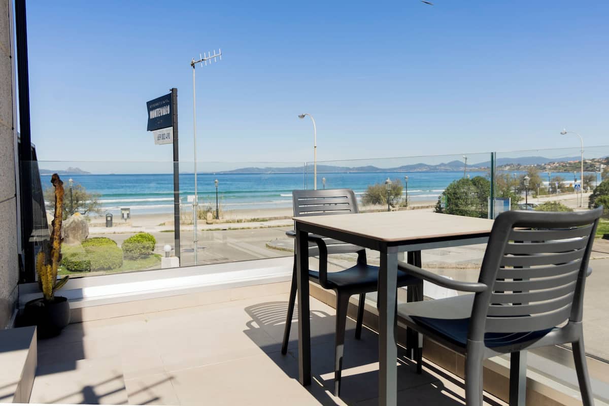 Varanda com mesa e cadeiras, vista para a praia e oceano.
