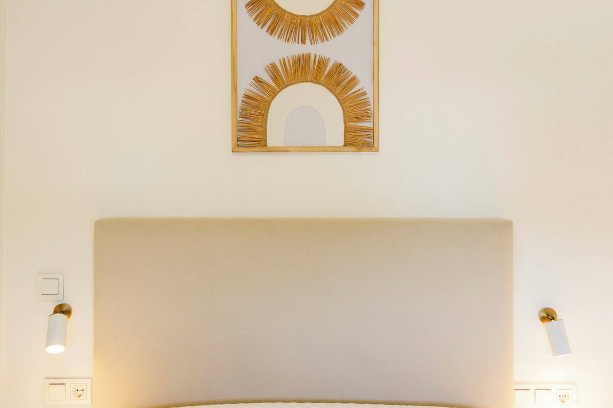 Cama com cabeceira branca e espelho fixado na parede com design em forma de sol.