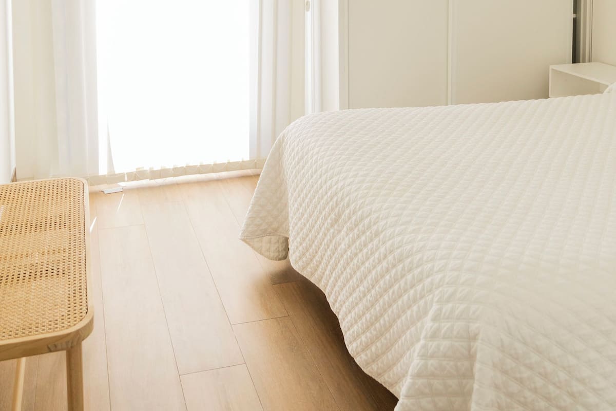 Quarto com cama, guarda-roupa, janela com persianas e cadeira de vime.