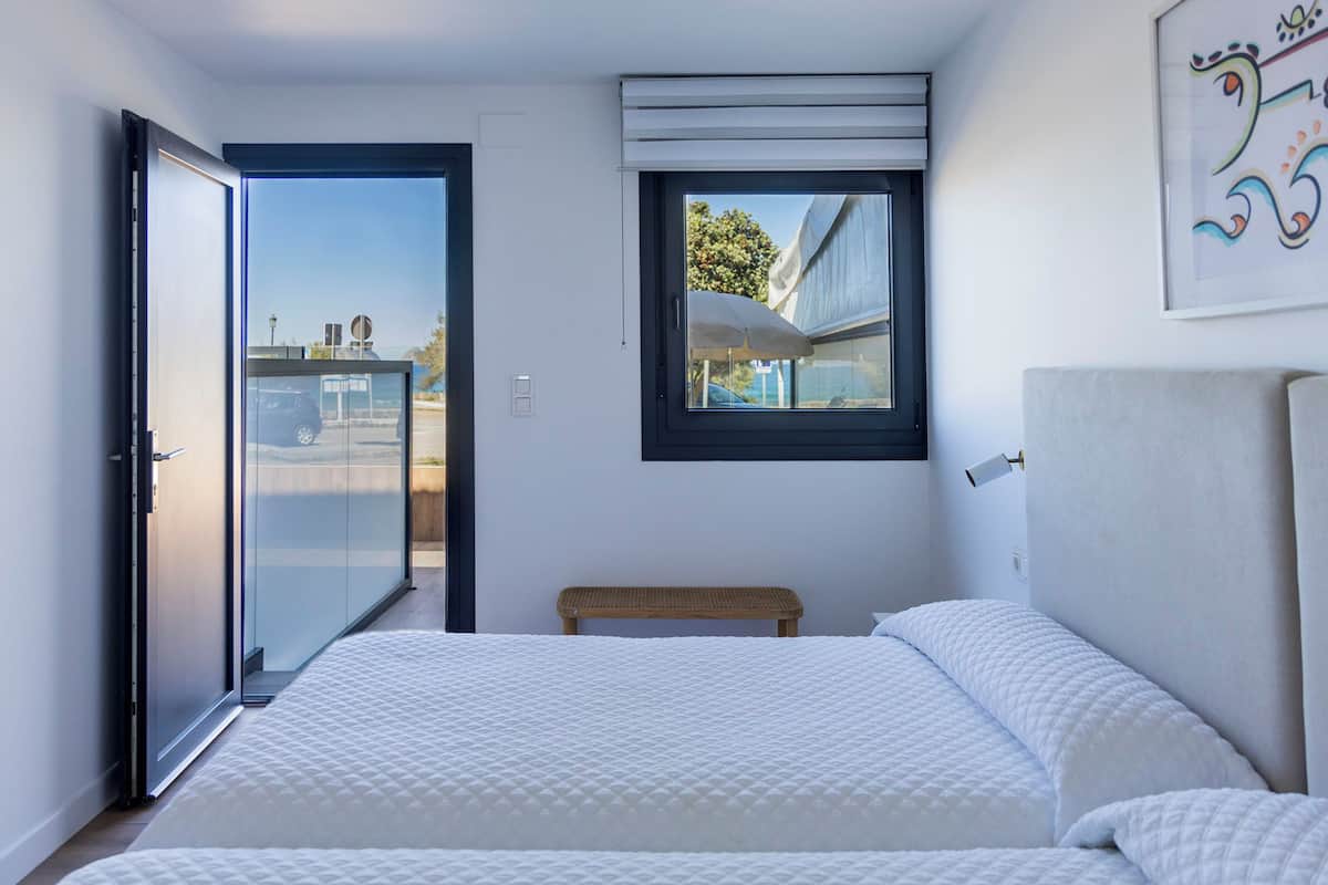 Quarto com cama, um banquinho, janela com vista e porta para área externa.