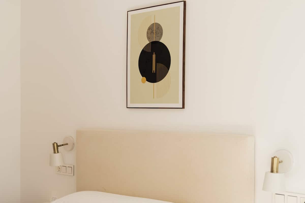 Quarto de hotel minimalista com cama, mesas de cabeceira e uma obra de arte na parede.