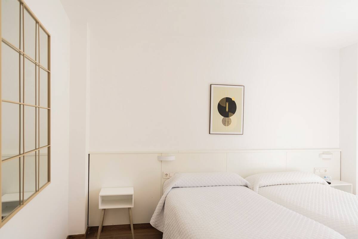 Quarto de hotel minimalista com cama, mesa de cabeceira e um quadro na parede.