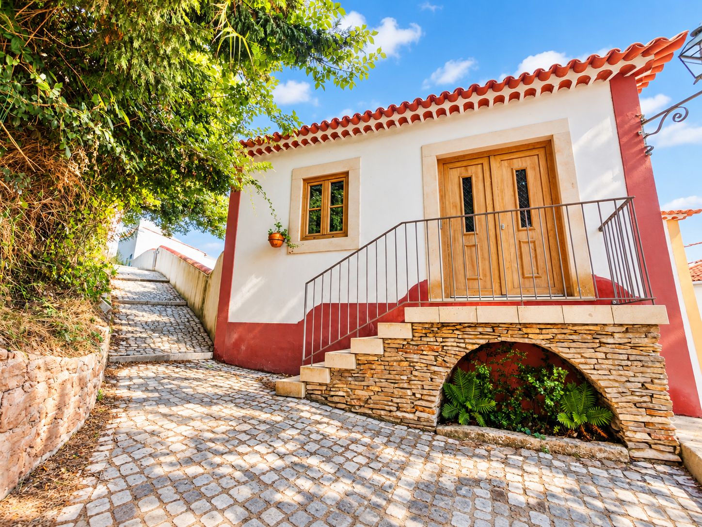 Um edifício com fachada vermelha e branca, escadaria de pedra e pequeno arco com folhagem.