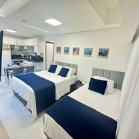 Quarto de hotel com duas camas, cozinha compacta e área de refeições.