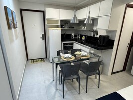 Cozinha compacta com armários brancos, bancada preta e mesa de jantar de vidro com cadeiras.