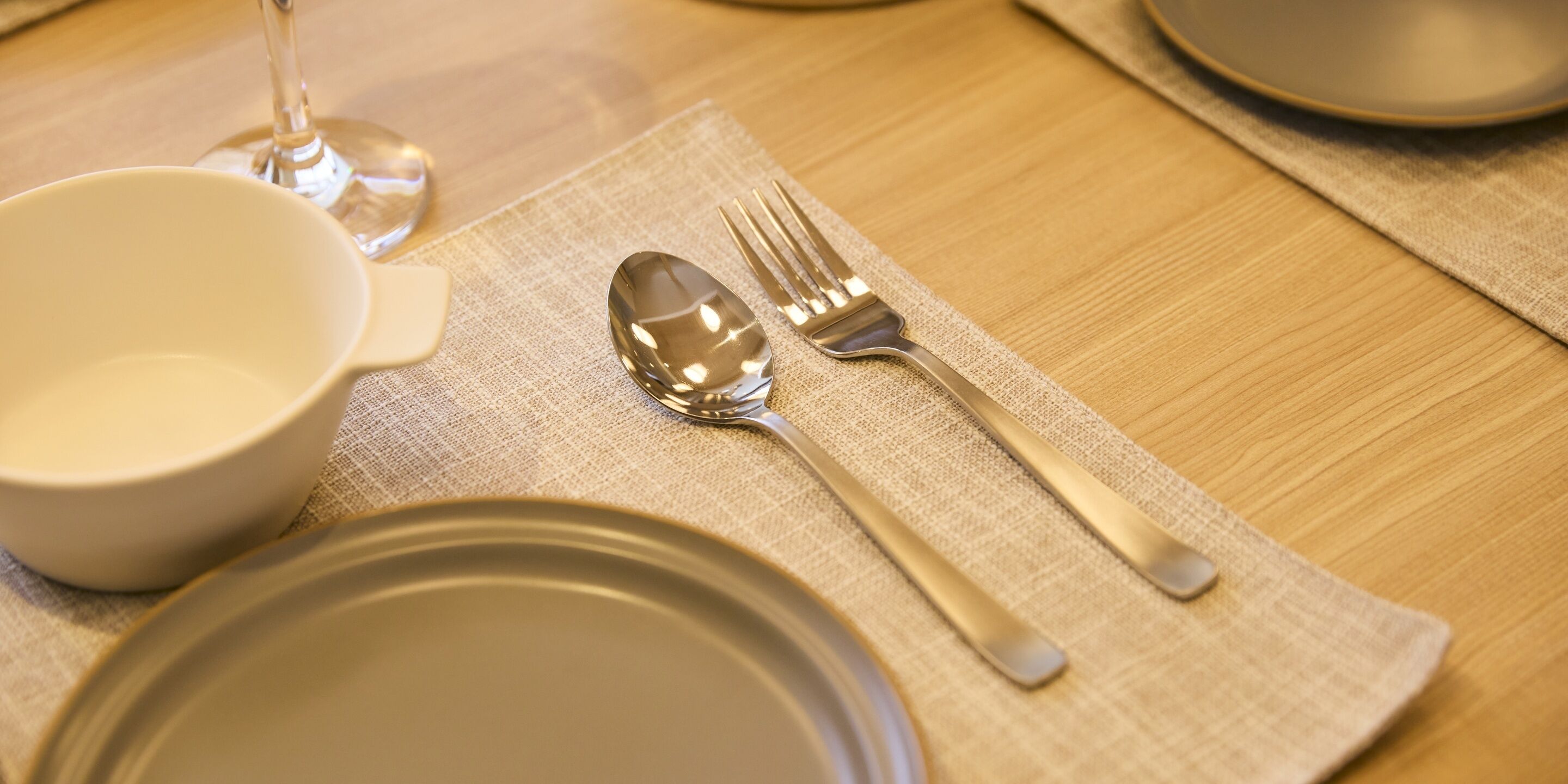 Uma mesa de jantar com uma tigela, uma colher e um garfo sobre um jogo americano.