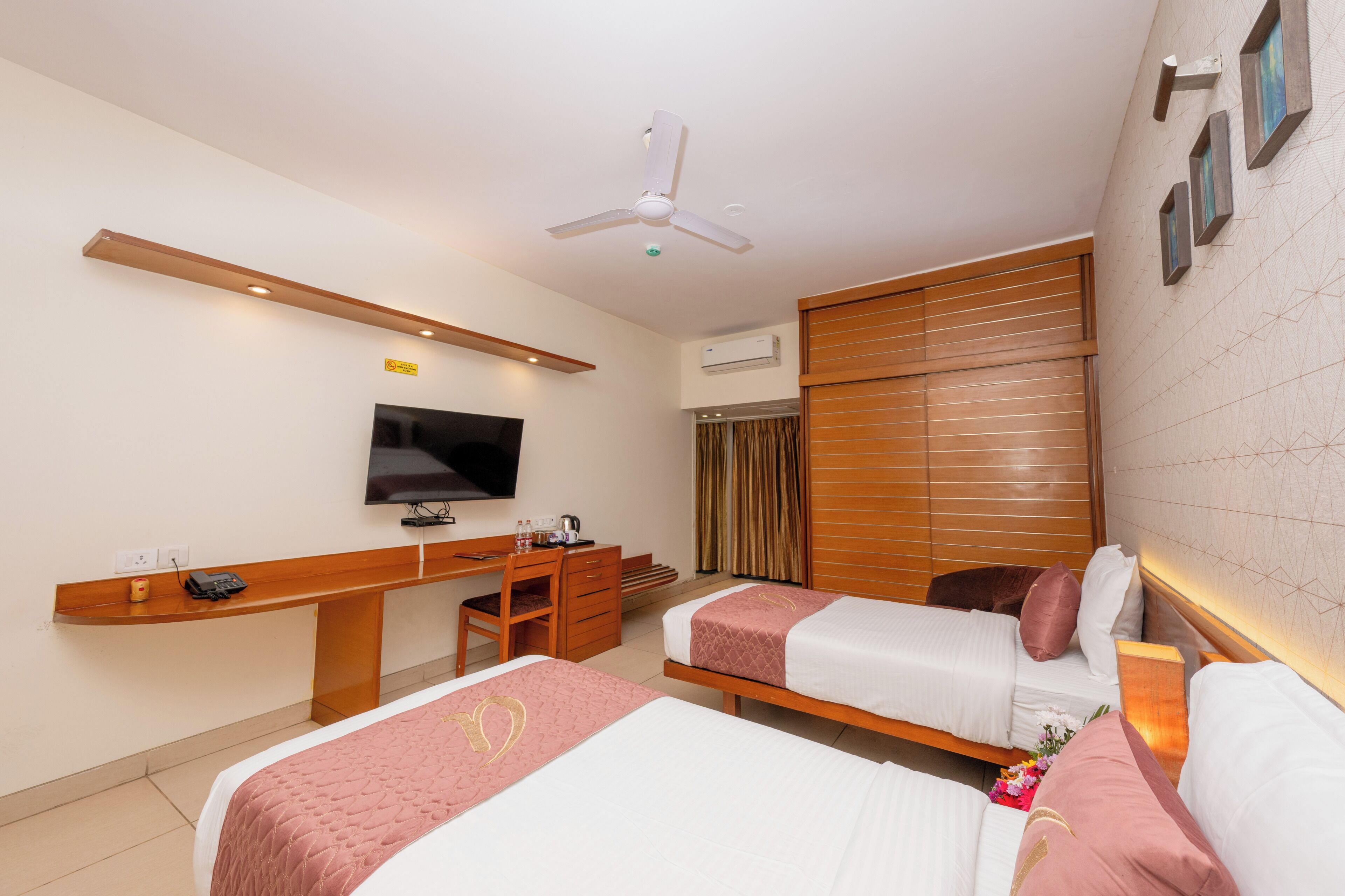 Quarto de hotel com duas camas, uma escrivaninha, uma televisão e um ventilador de teto.