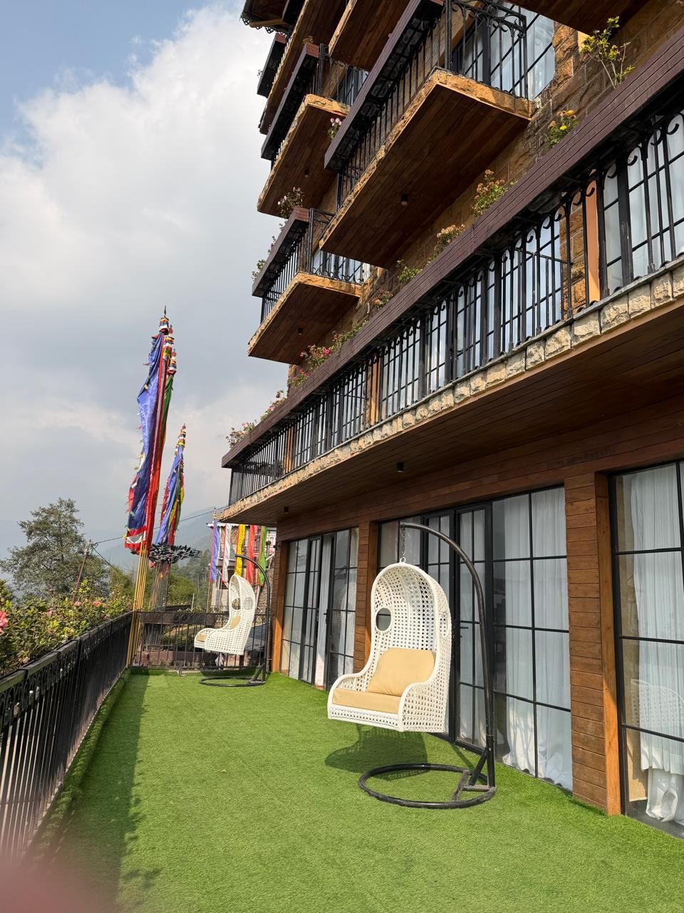 Um hotel com varandas de madeira, janelas amplas e um gramado artificial verde.
