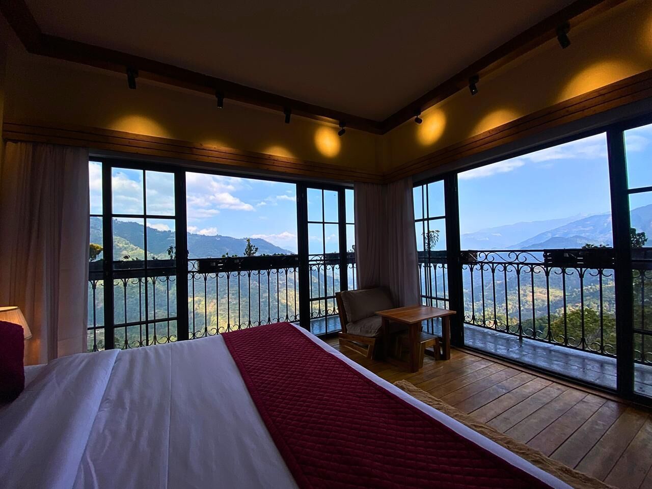 Quarto com uma cama grande, uma cadeira, uma mesa pequena e uma varanda com vista para as montanhas.