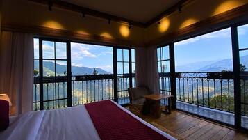 Quarto com uma cama grande, uma cadeira, uma mesa pequena e uma varanda com vista para as montanhas.
