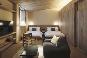 Quarto de hotel com duas camas, um sofá, uma TV e um abajur.