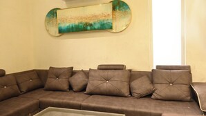 Um sofá modular com várias almofadas, uma mesa de centro e uma obra de arte abstrata na parede.