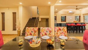 Uma sala de jantar com uma mesa posta para quatro pessoas, uma escada e uma cozinha ao fundo.