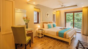 Quarto de hotel com cama, escrivaninha, cadeira e vista para o verde lá fora.