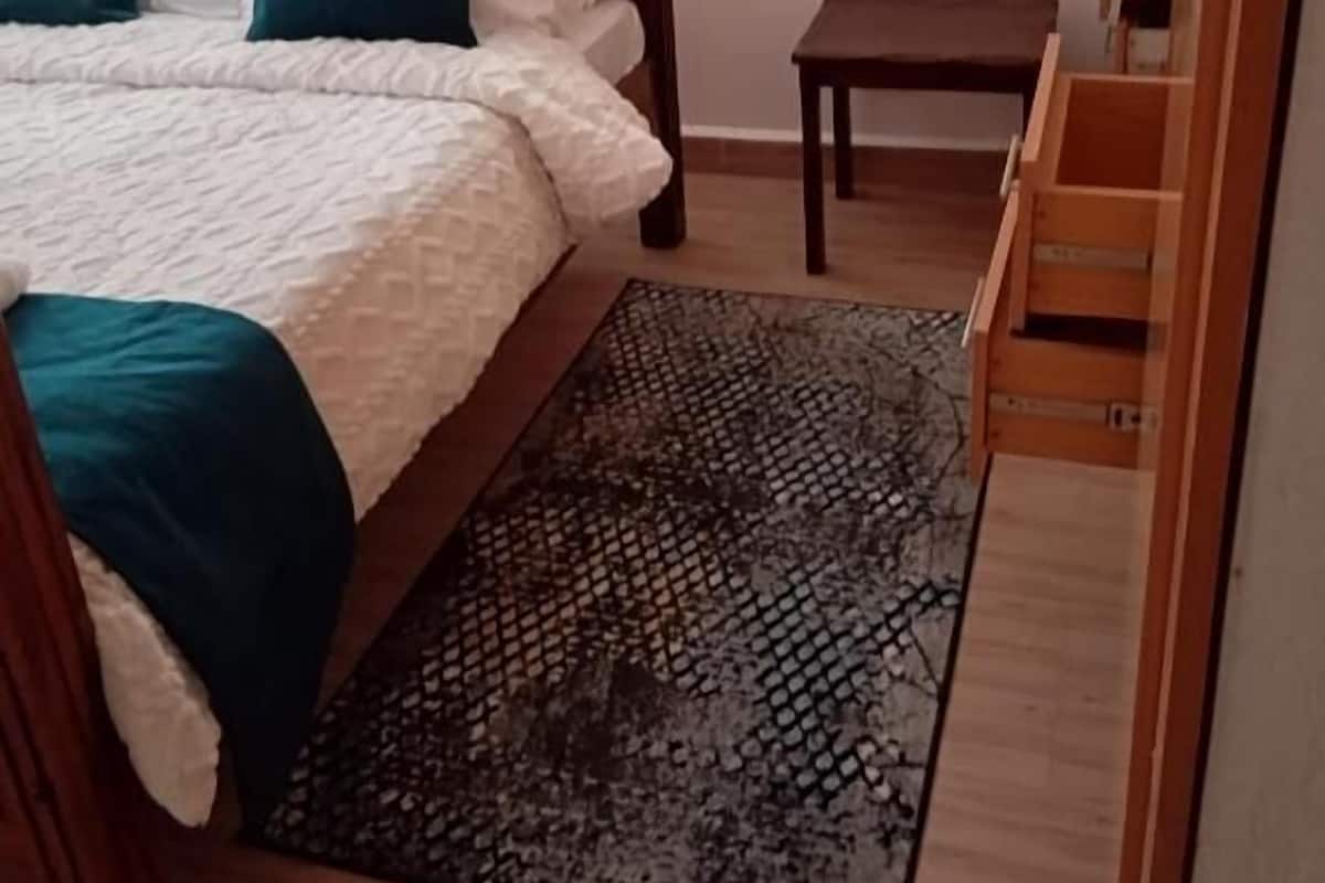 Um quarto com uma cama, uma janela com persianas, uma mesa pequena e um lance de escada de madeira.