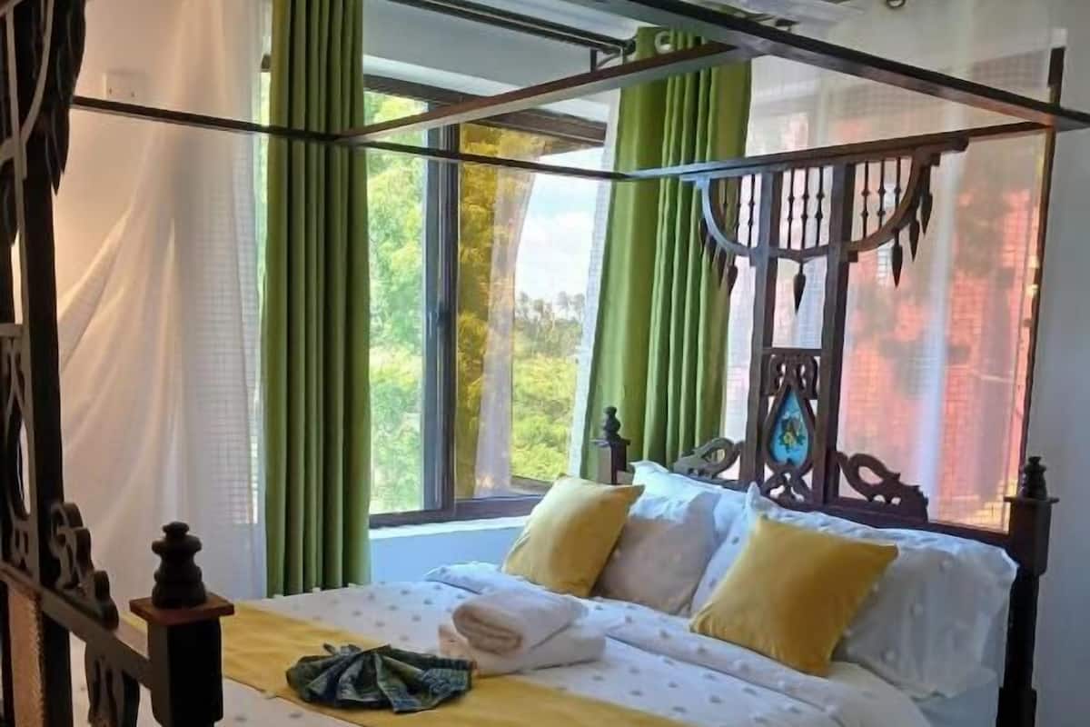 Uma cama com dossel, cortinas verdes e vista para o verde lá fora.