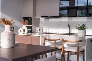 Uma cozinha moderna com bancadas de mármore, uma mesa de jantar de madeira, dois bancos altos e vasos decorativos.