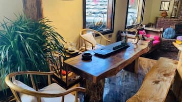 Uma mesa de madeira com um teclado, uma planta e um banco em um quarto com janela.