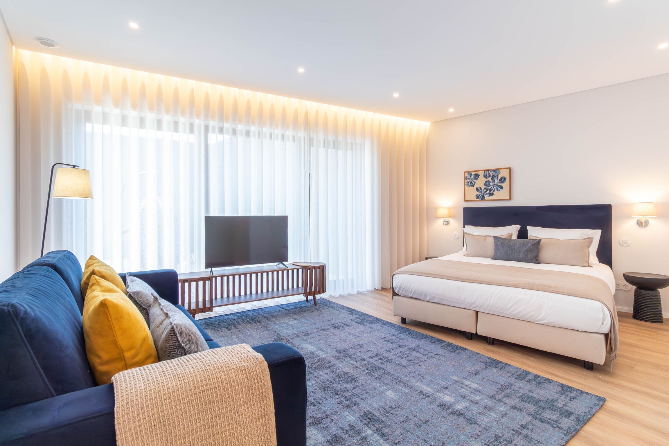 Quarto de hotel moderno com uma cama grande, um sofá, uma televisão e uma escrivaninha.