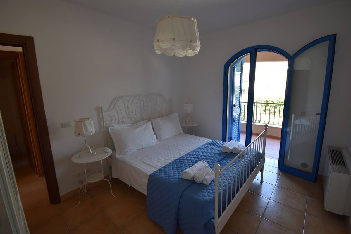 Quarto com cama, mesas de cabeceira, espelho e varanda.